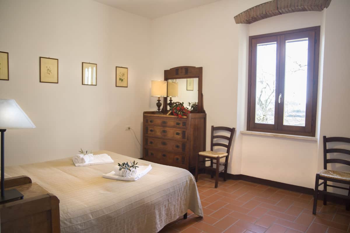 Quarto com cama, penteadeira, cadeiras e janela.