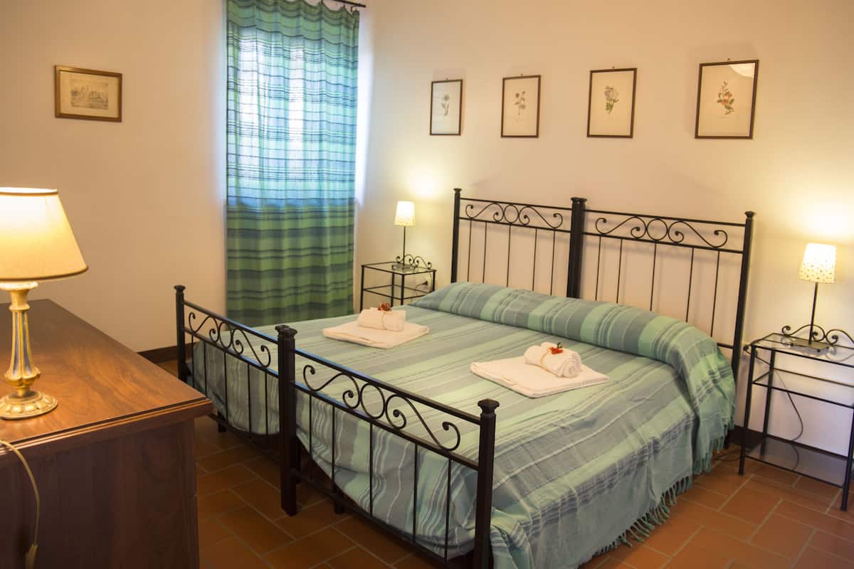 Cama bem arrumada com colcha listrada e dois travesseiros, com duas mesas de cabeceira e abajures ao lado.