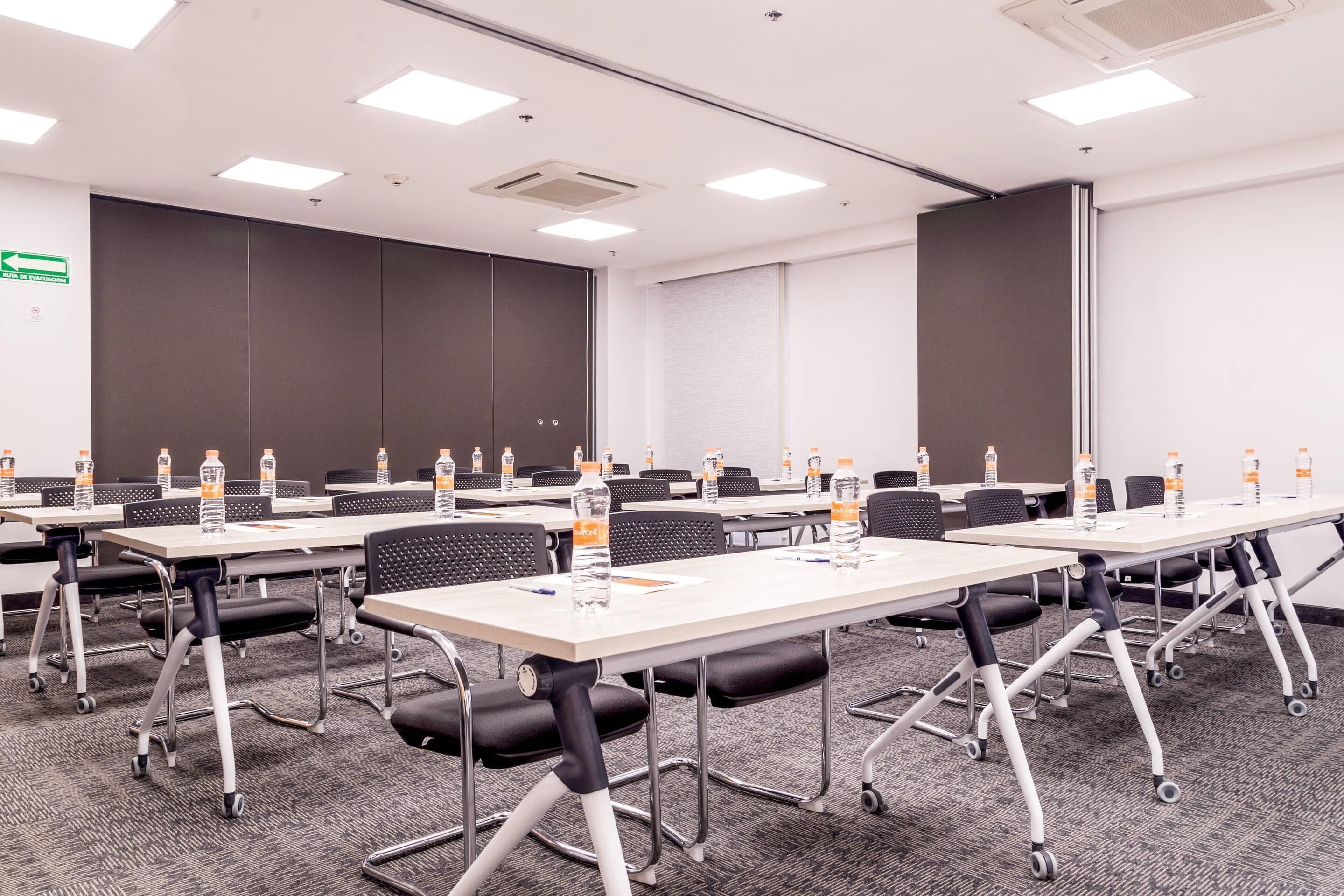Uma sala de conferências com várias mesas, cadeiras e garrafas de água.