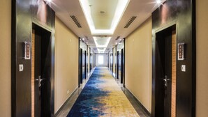 Corredor de hotel com um tapete comprido, portas em ambos os lados e iluminação no teto.
