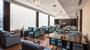 Um hall de hotel moderno com áreas de estar, um bar e janelas amplas.