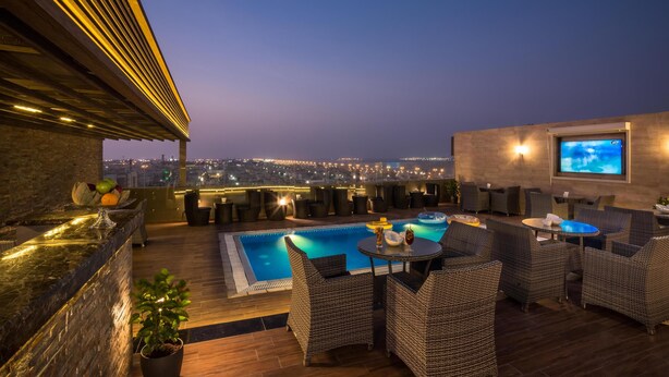 Um bar no terraço com piscina, mobiliário de vime e uma tela de televisão.