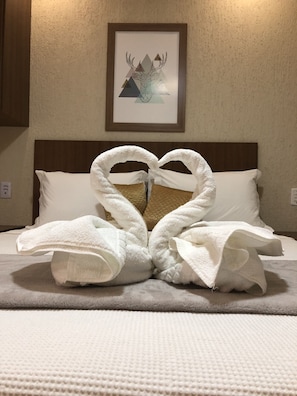 Uma cama com toalhas dispostas em formato de coração, uma obra de arte emoldurada na parede e um espalha-cama texturizado.
