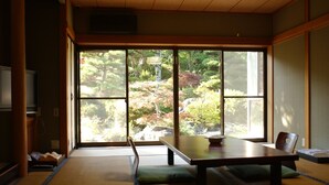 Um quarto japonês tradicional com tatames, uma mesa baixa e vista para um jardim através de amplas janelas.