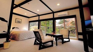 Quarto com uma cama, duas cadeiras, uma mesa pequena e uma televisão.