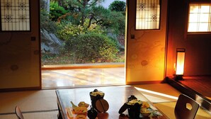 Um quarto japonês tradicional com tatames, uma mesa de madeira baixa com chá e vista para um jardim através de biombos shoji.