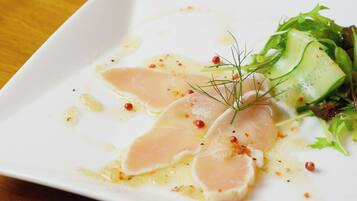 Um prato branco com fatias finas de peixe, um raminho de endro e uma guarnição de folhas verdes frescas.