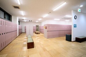 Vestiário com vários armários, um banco de madeira e uma lixeira.
