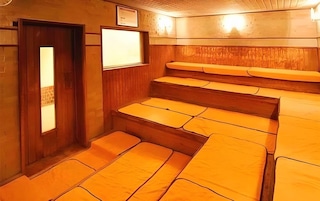 Quarto com paredes de madeira e uma porta, apresentando um conjunto de degraus que levam a um espaço de estar com bancos acolchoados.