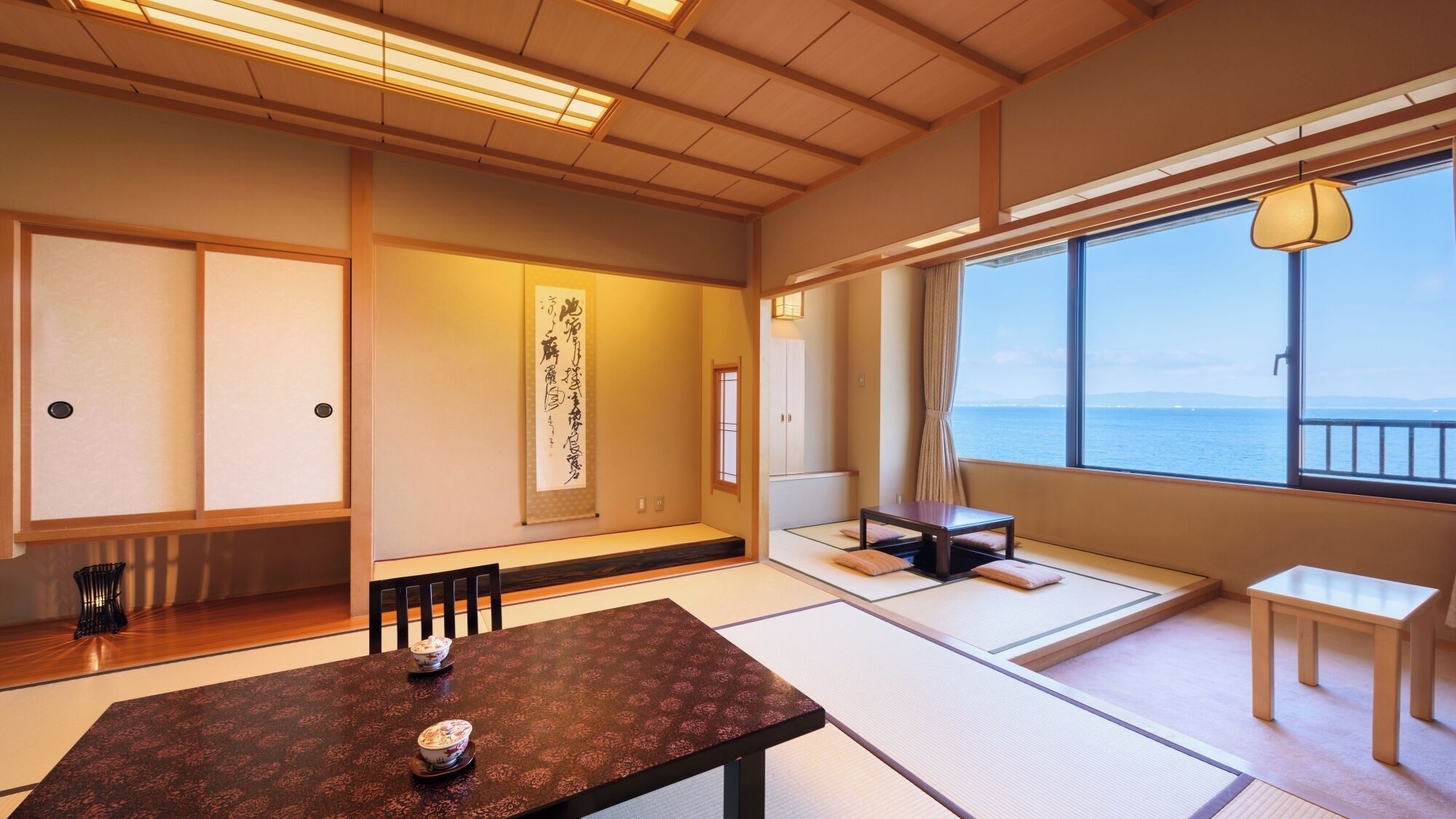Um quarto japonês tradicional com tatames, uma mesa baixa com uma tigela, uma porta deslizante e vista para o mar.
