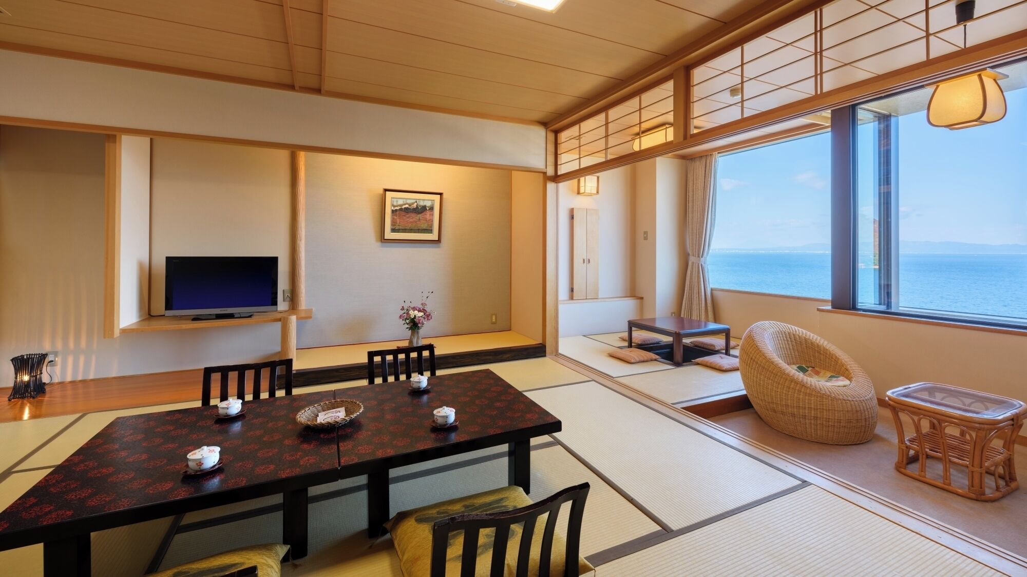 Quarto tradicional japonês com tatames, uma mesa baixa com almofadas, televisão e vista para o mar.