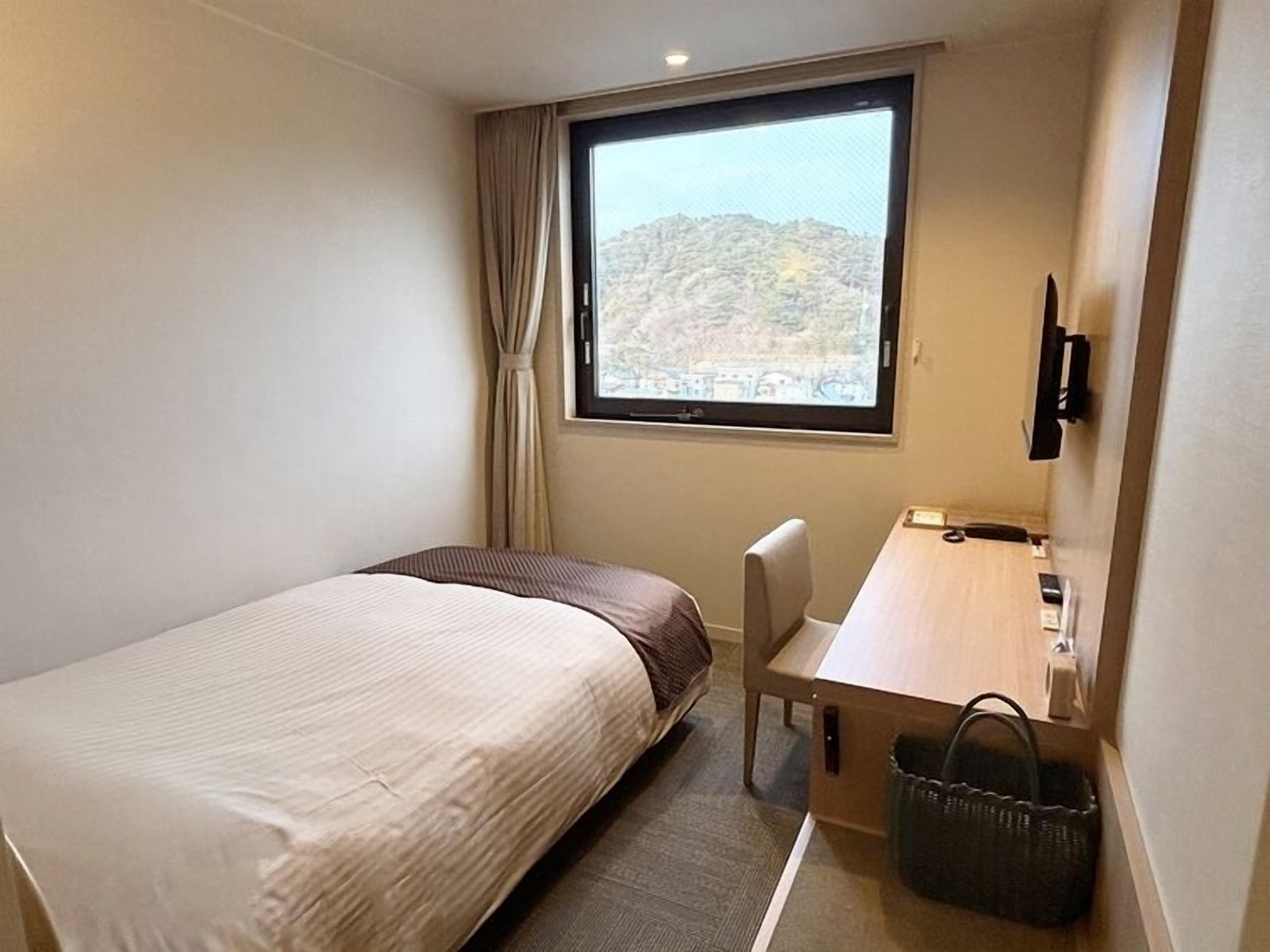 Quarto de hotel com uma cama, uma escrivaninha, uma cadeira, uma TV e uma janela com vista para uma montanha.