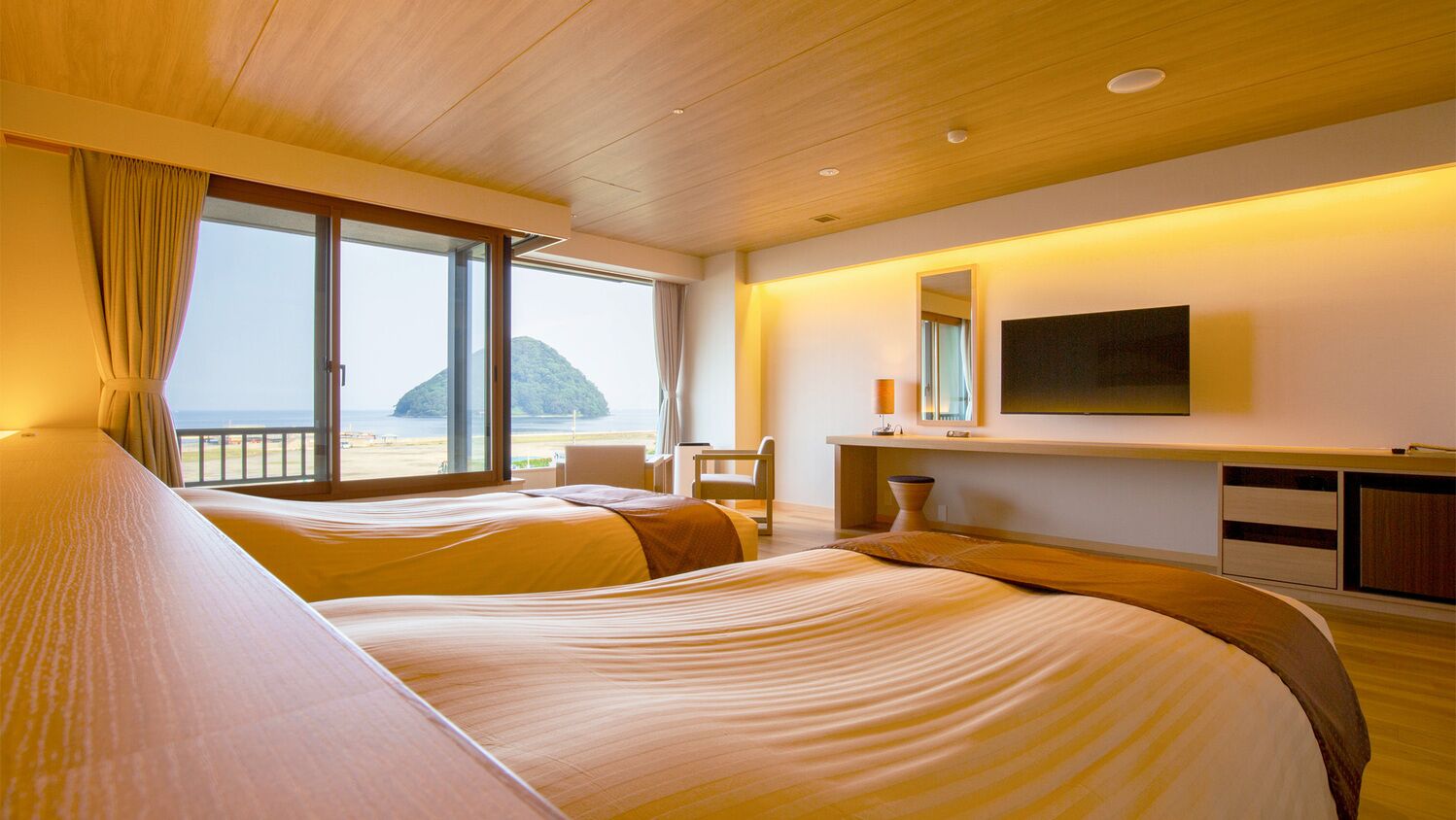 Quarto de hotel com uma cama grande, uma mesa, uma cadeira, uma televisão e vista para o mar.