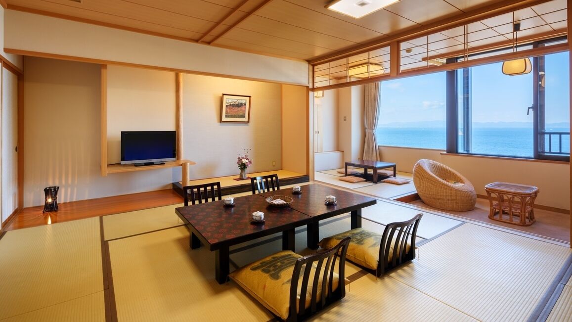 Quarto japonês tradicional com tatames, uma mesa baixa com almofadas, televisão e vista para o mar.