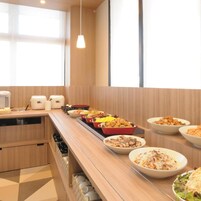 Disposição de buffet com diversos pratos, máquina de café e luminária pendente.