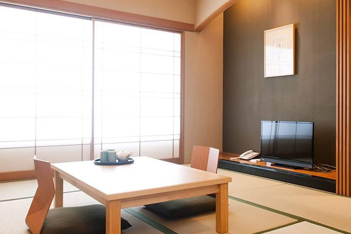 Um quarto japonês tradicional com tatames, uma mesa baixa, um sofá e uma TV sobre um suporte.