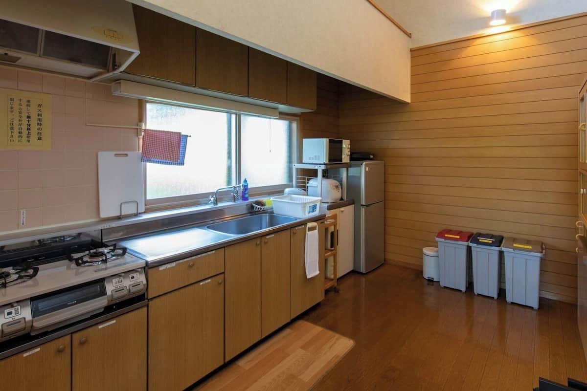 Cozinha compacta com armários de madeira, pia de aço inoxidável, fogão a gás, micro-ondas e geladeira.