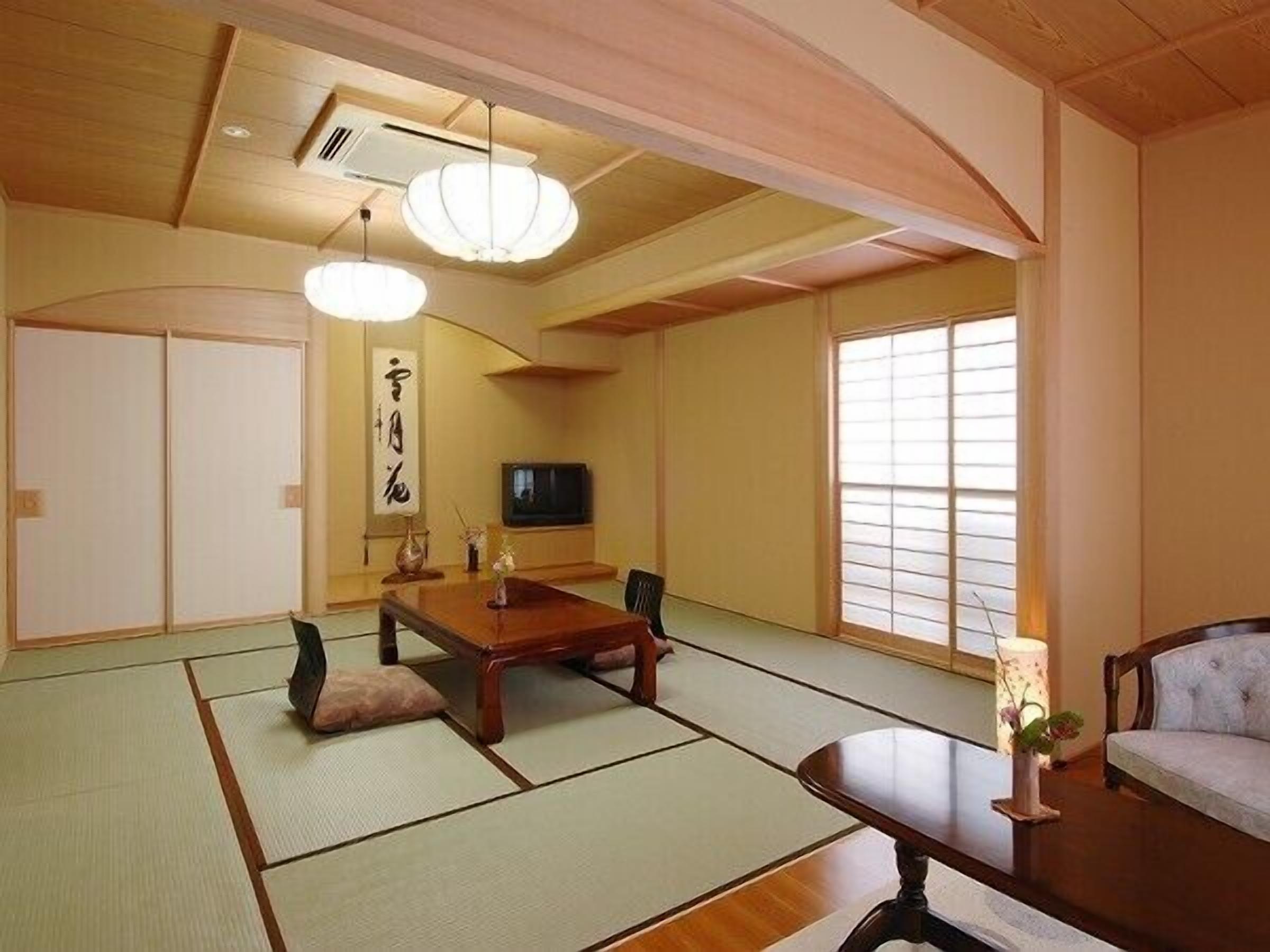 Um quarto japonês tradicional com tatames, uma mesa baixa, um sofá e uma televisão.
