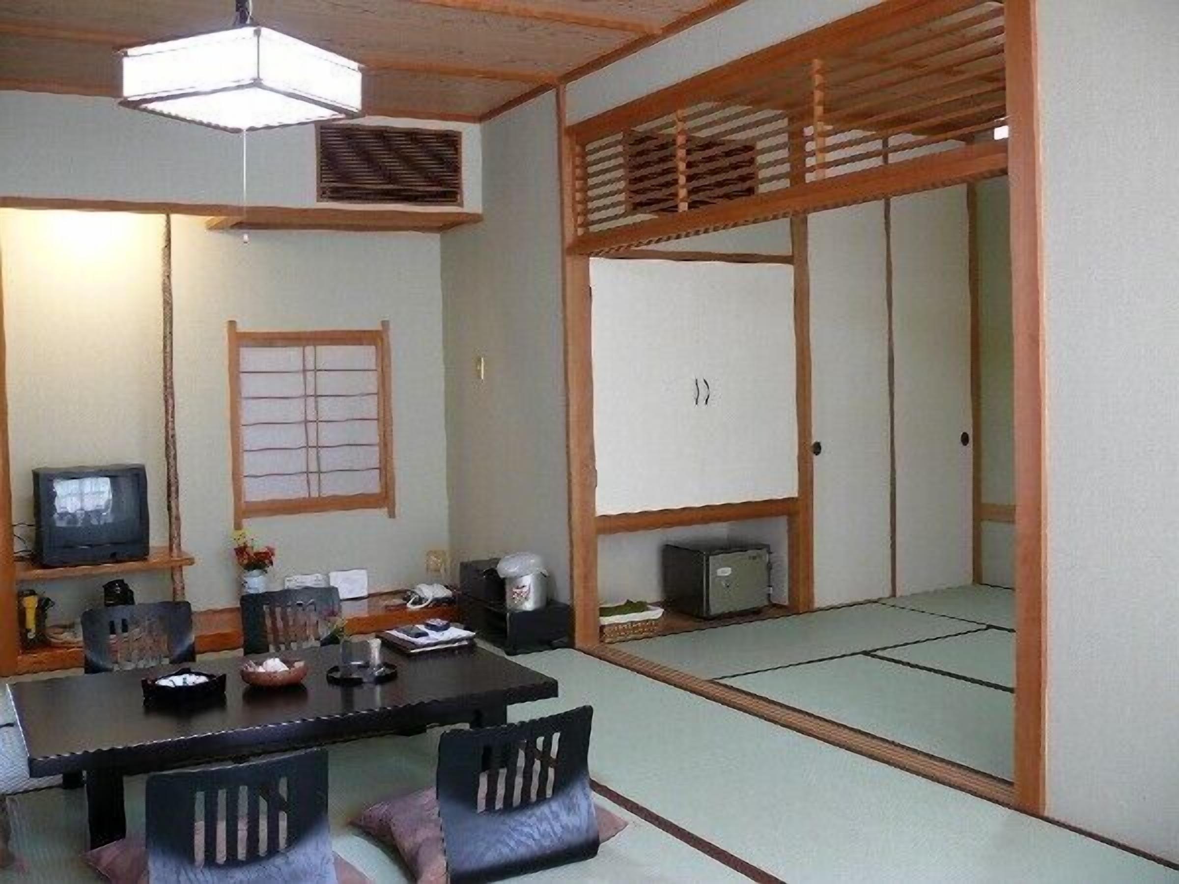 Um quarto tradicional japonês com tatames, uma mesa baixa com cadeiras, uma televisão e uma porta deslizante.