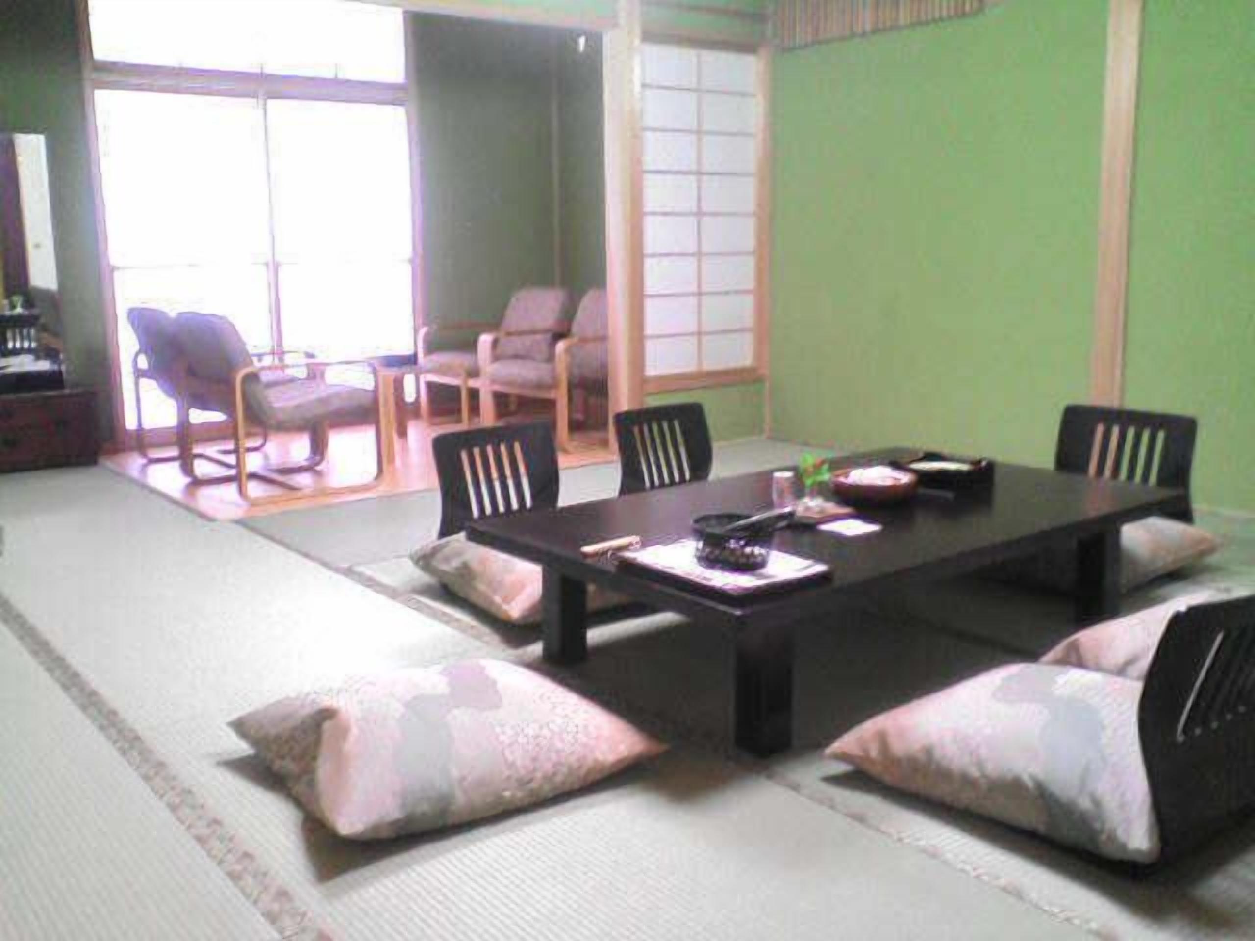 Um espaço com esteiras de tatame, uma mesa baixa, cadeiras e vista para um quarto japonês tradicional.