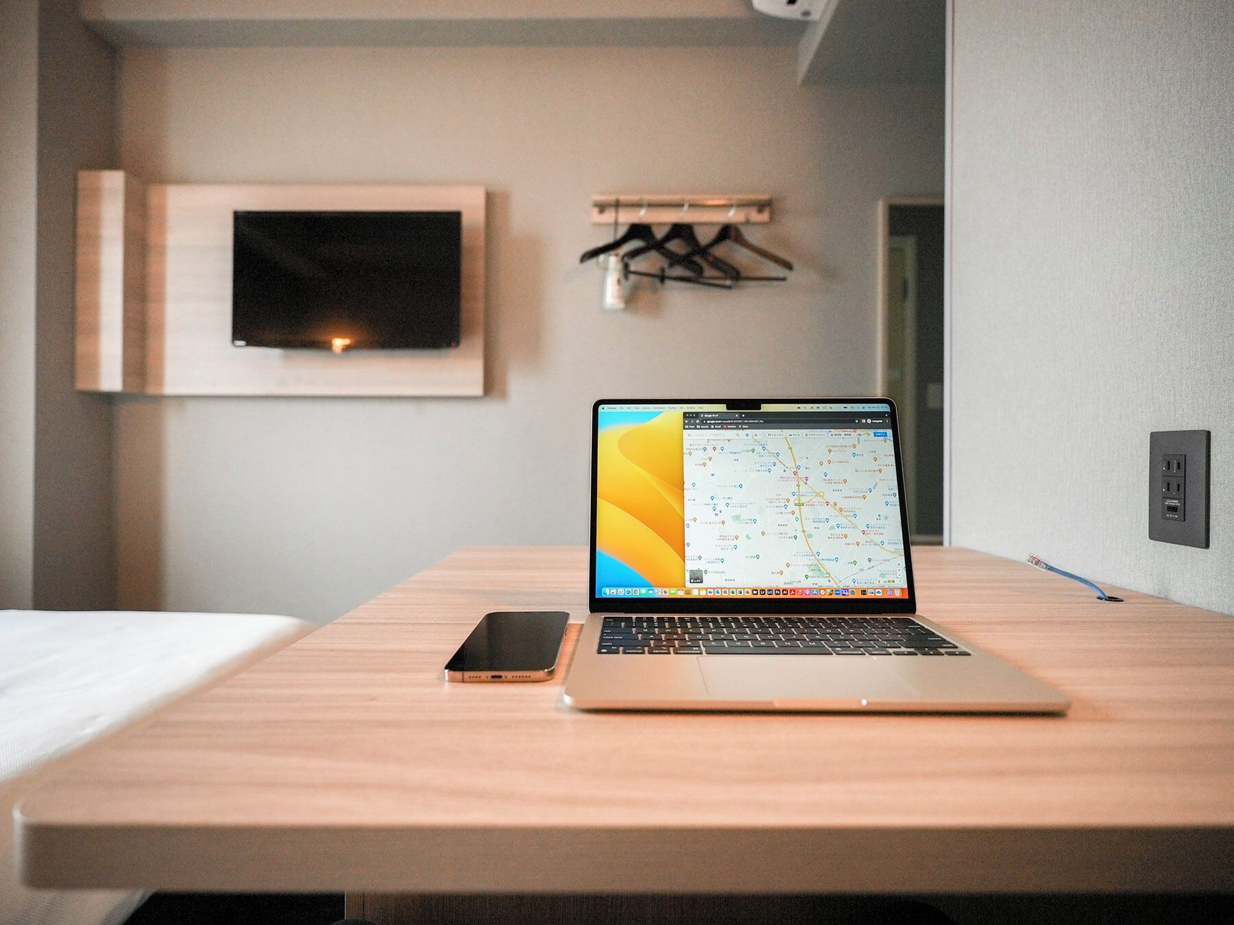 Quarto de hotel com uma secretária de madeira, um laptop e um smartphone.