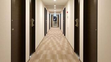 Corredor longo e estreito de hotel com assoalho de madeira e portas escuras em ambos os lados.