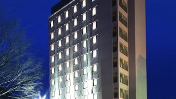 Um hotel moderno com fachada imponente, vários andares e janelas iluminadas.