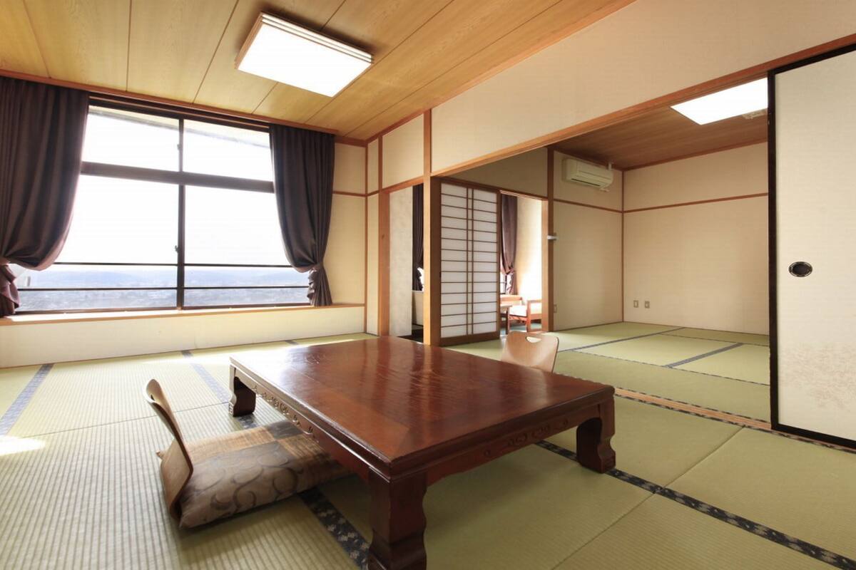 Um quarto japonês tradicional com tatames, uma mesa de madeira, um futon, portas deslizantes e uma janela com cortinas.