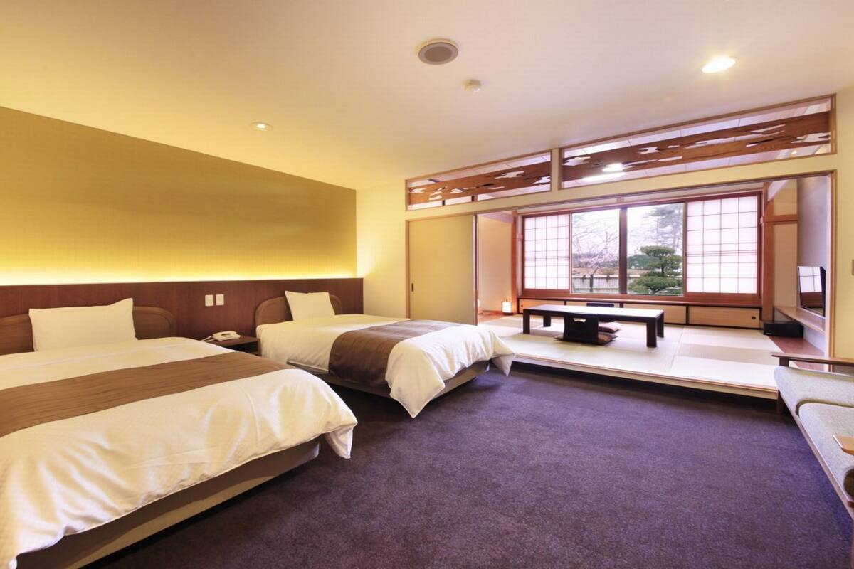 Quarto de hotel com duas camas, um banco, piso de tatame e uma grande janela com vista.
