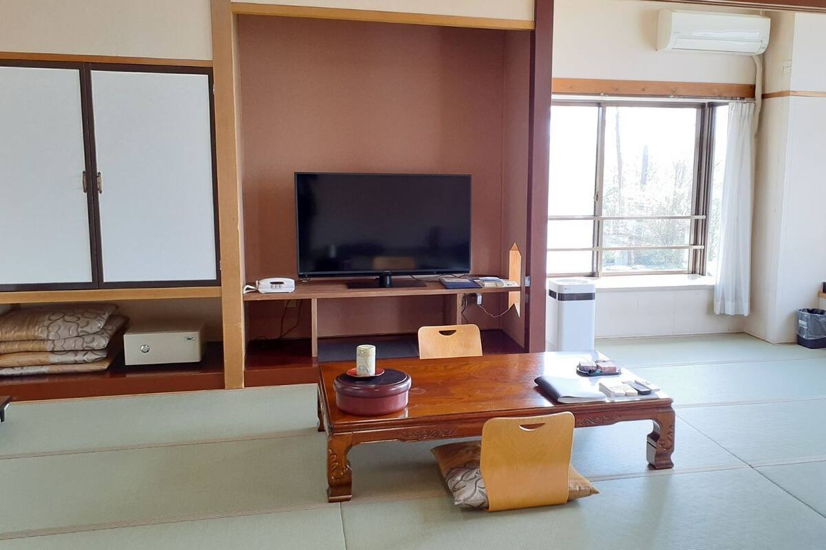 Um quarto japonês tradicional com tatames, uma televisão, uma mesa de madeira e um portas correderas.