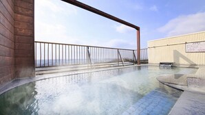 Uma piscina de águas termais com um deck de madeira e guarda-corpo de metal, com vista para um corpo d'água.