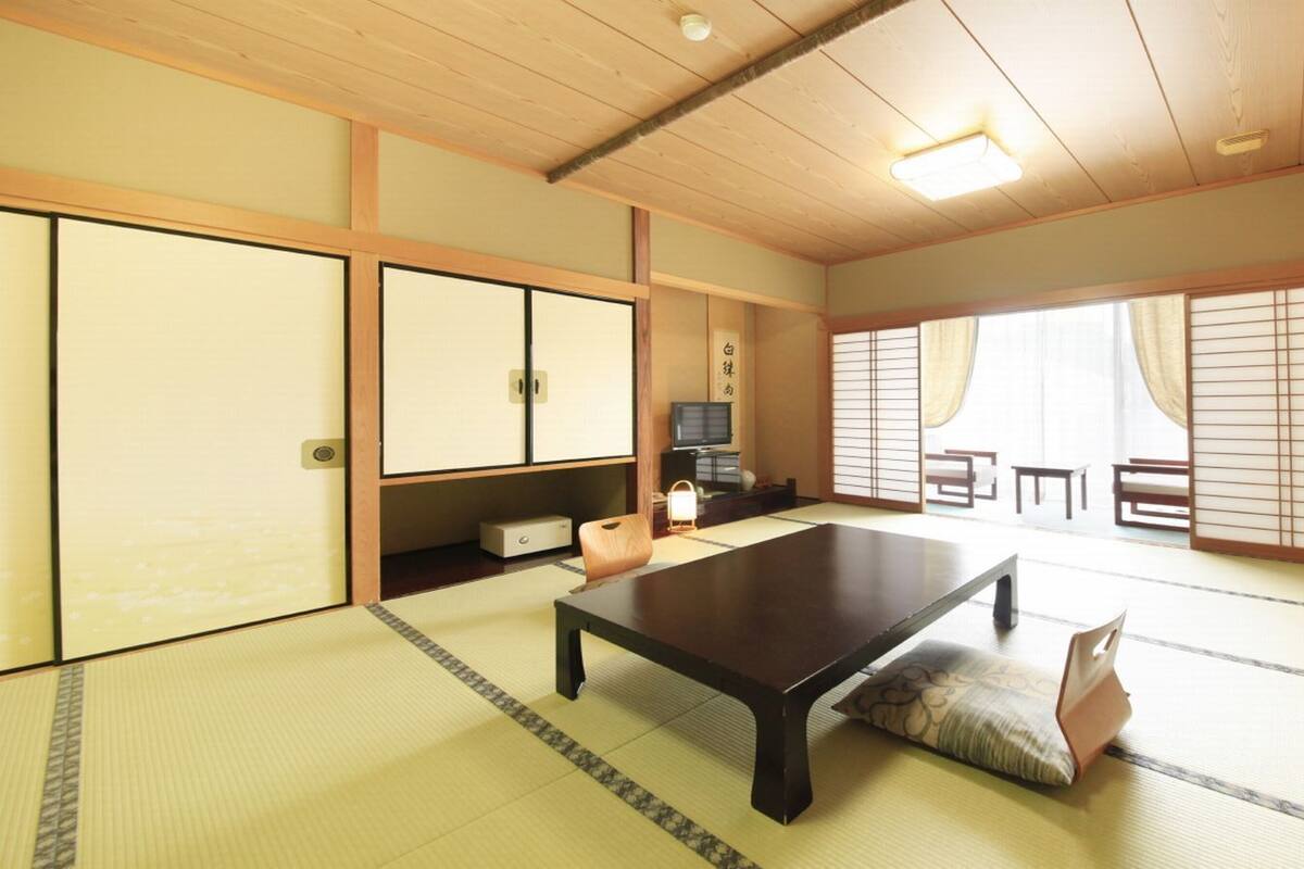 Um quarto japonês tradicional com tatames, uma mesa baixa, portas deslizantes e uma televisão.