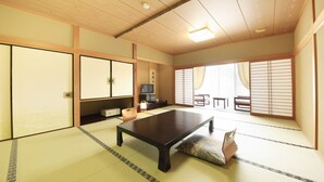 Um quarto japonês tradicional com tatames, uma mesa baixa, portas deslizantes e uma televisão.