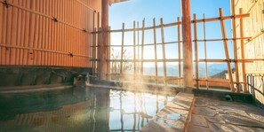 Uma onsen japonesa tradicional com interior de madeira, soalho de pedra e vista para as montanhas.