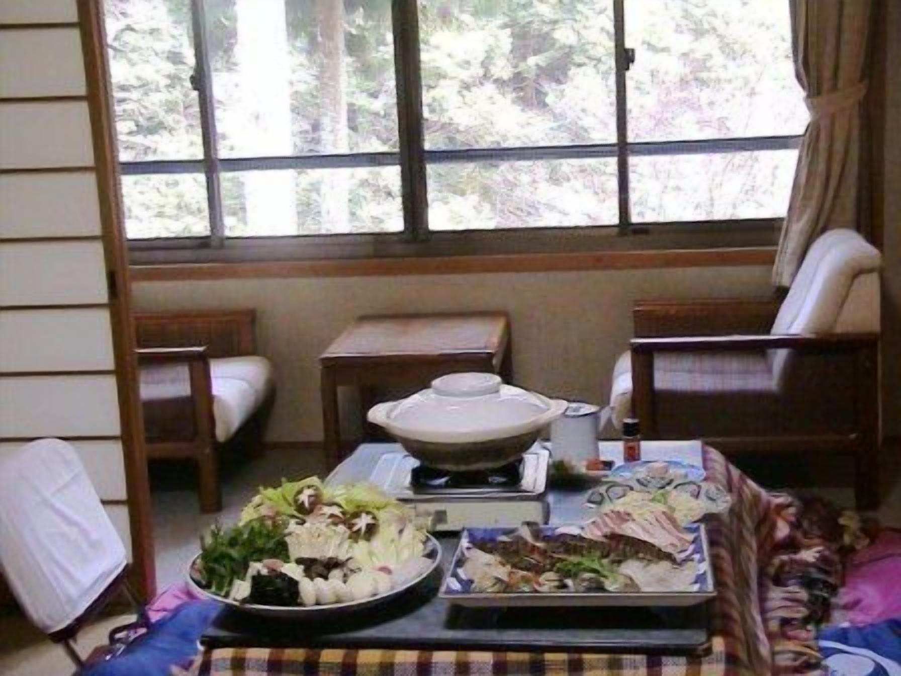 Uma área de refeições com uma mesa posta para refeição, uma janela com vista para árvores e um sofá.