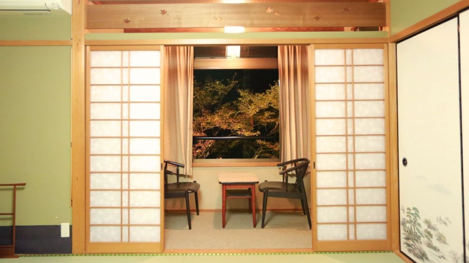 Um quarto japonês tradicional com tatames, uma mesa baixa, duas cadeiras e uma janela com vista para folhagem de outono.