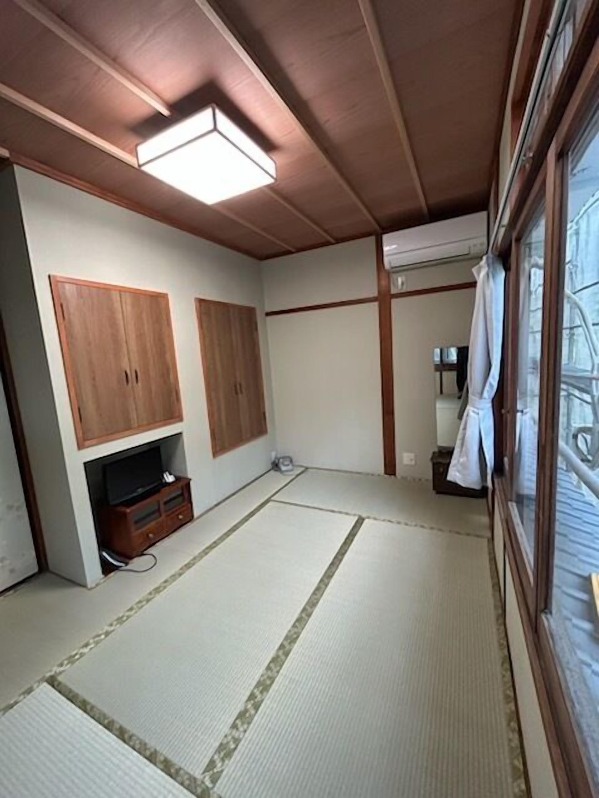 Quarto com tatames, armários de madeira, televisão e janela com cortina.