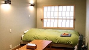 Quarto compacto com cama, uma mesinha, um banco e uma janela.