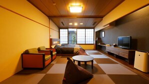 Quarto de hotel com sofá, mesa pequena, televisão e janela com vista.