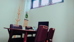 Sala de conferência com mesa, quatro cadeiras, calendário, planta e janela com a inscrição 'THE STAY'.