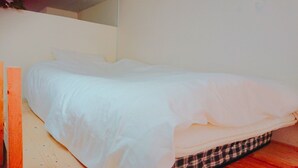 Uma cama com roupa de cama branca e manta xadrez.