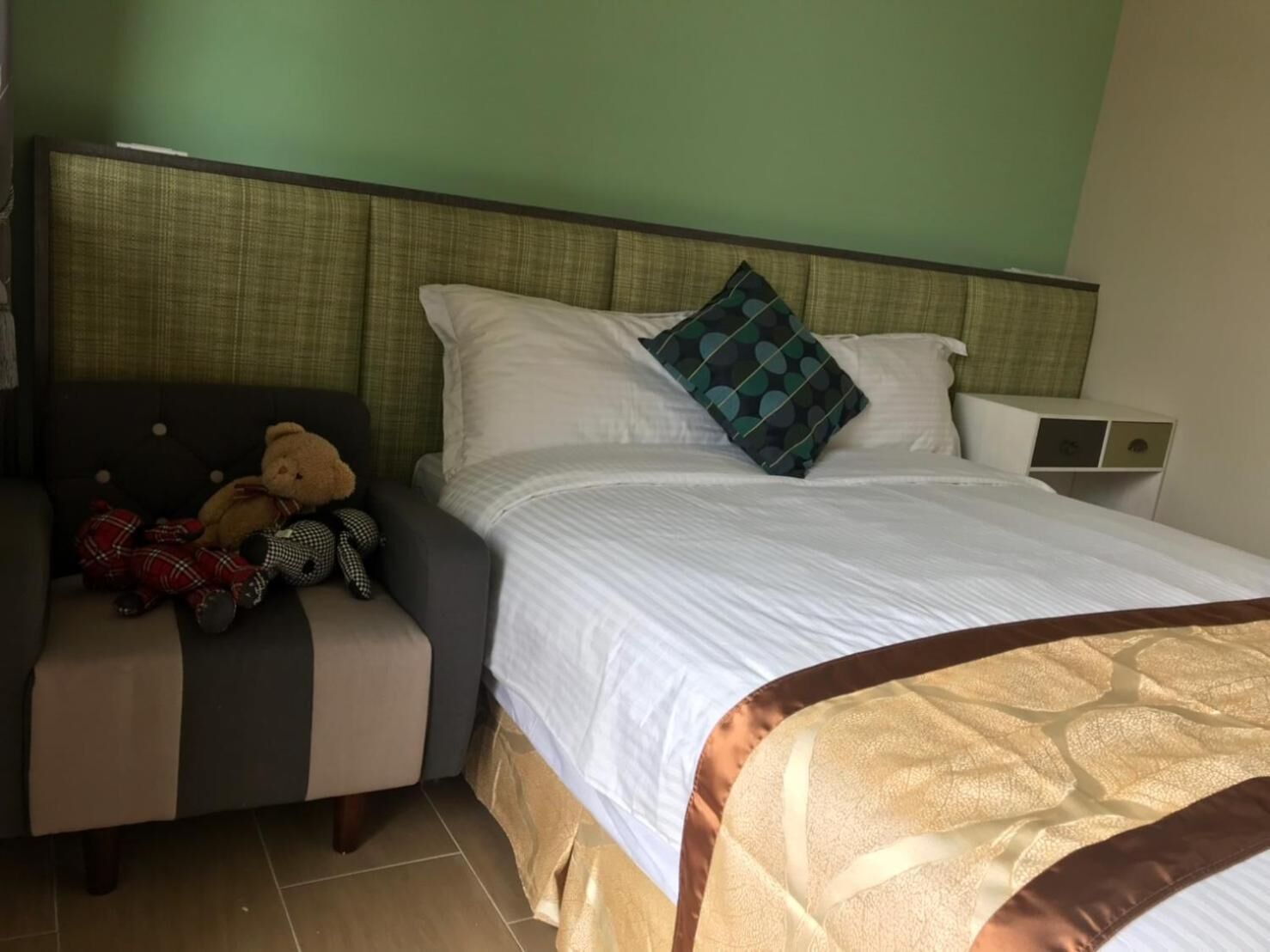 Quarto de hotel com uma cama, mesa de cabeceira, cadeira e um ursinho de pelúcia.