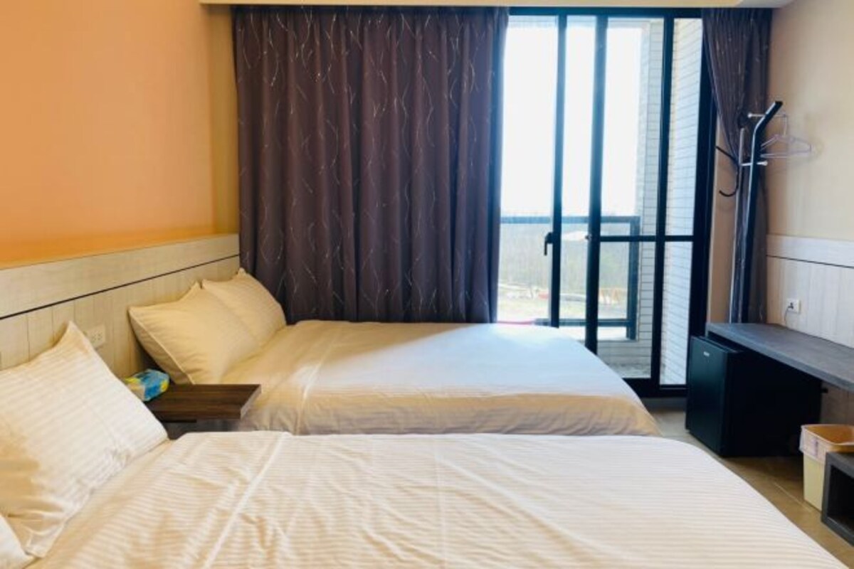 Quarto de hotel com duas camas, uma escrivaninha pequena e vista para o exterior através de uma grande janela.