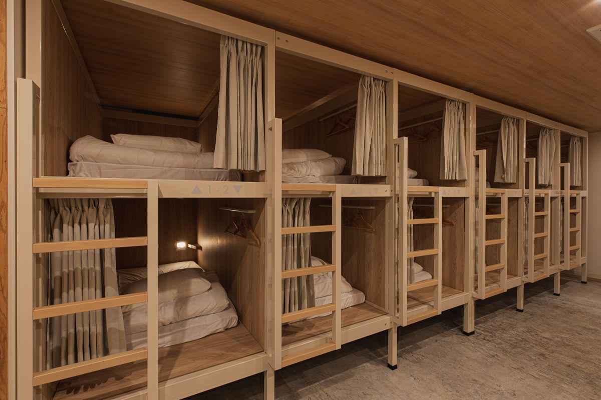 Uma fileira de beliches com estrutura de madeira e cortinas, dispostos em um único quarto.