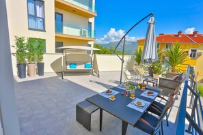 Terraço no telhado com mesa de jantar posta para dois, móveis de exterior, plantas em vasos e vista para a paisagem urbana.
