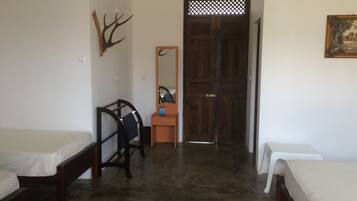 Quarto com duas camas de solteiro, uma cadeira de madeira, uma mesinha com um espelho e uma grande porta de madeira.