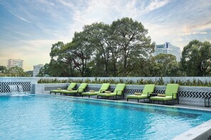 Piscina com cadeiras de descanso verdes e parede estampada.