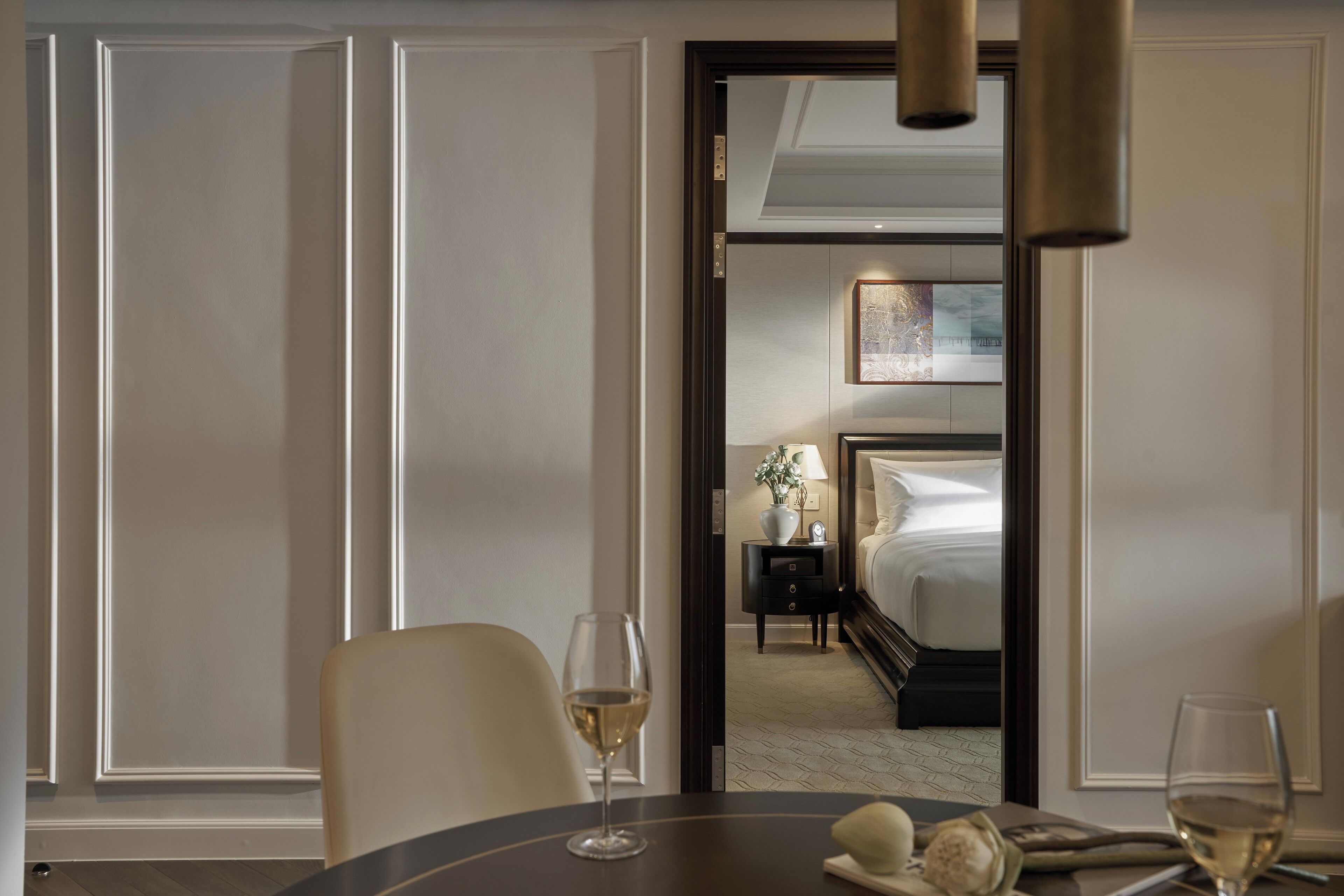 Quarto de hotel com área de refeições, cama e mesa de cabeceira com abajur.