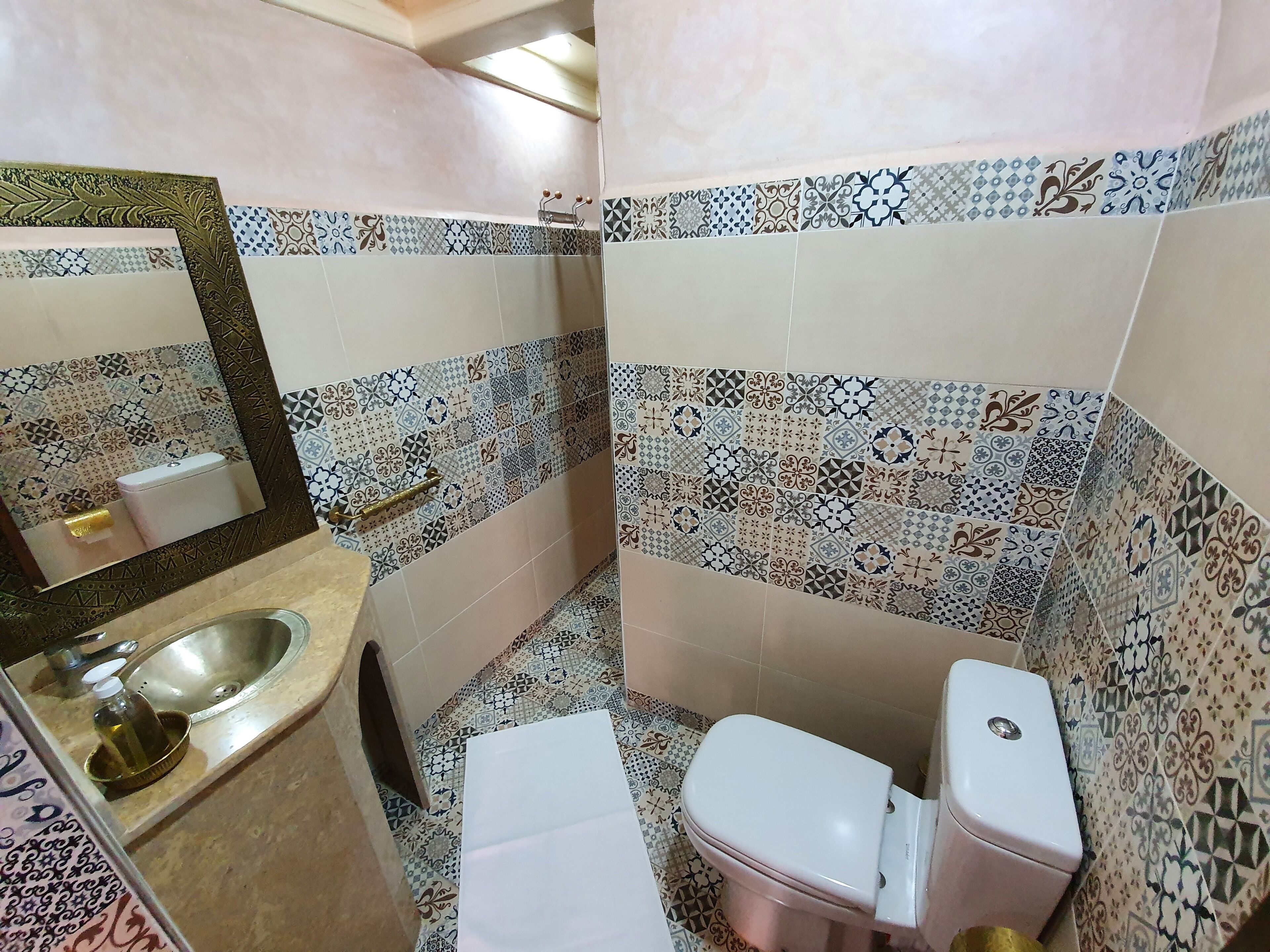 Casa de banho com azulejos estampados, uma pia e duas sanitas.