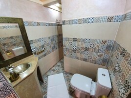 Casa de banho com azulejos estampados, uma pia e duas sanitas.